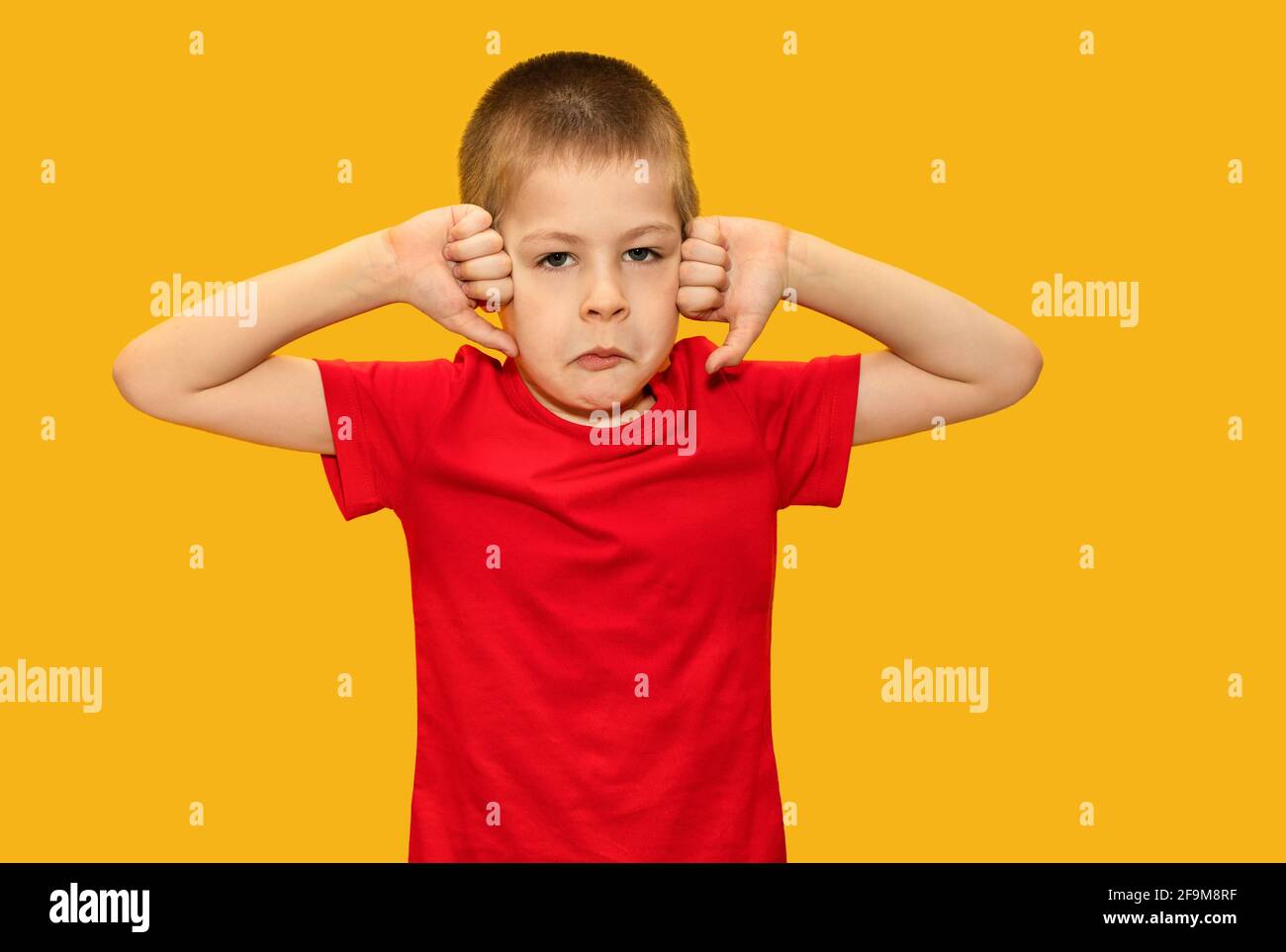 Child in red t-shirt on yellow background, boy 5 years old, sad. Shows ...