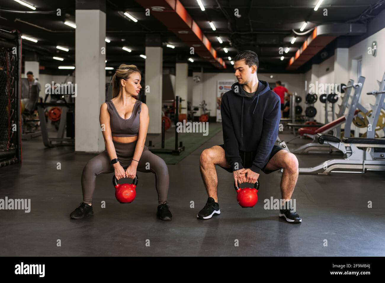 Personal trainer shows a woman how to squat with a kettlebell in a ...