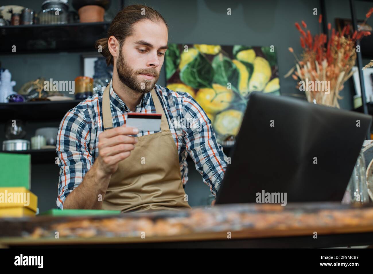 Bearded salesman using wireless laptop at decor store for registration ...