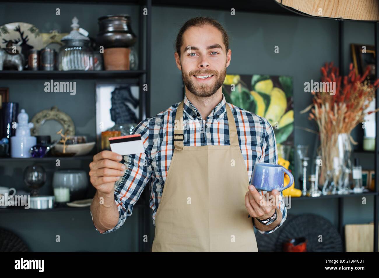 Positive bearded man holding ceramic cup and discount card in hands ...