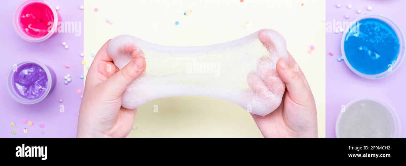 Multi-colored slimes on the table. A child plays with a white slime ...