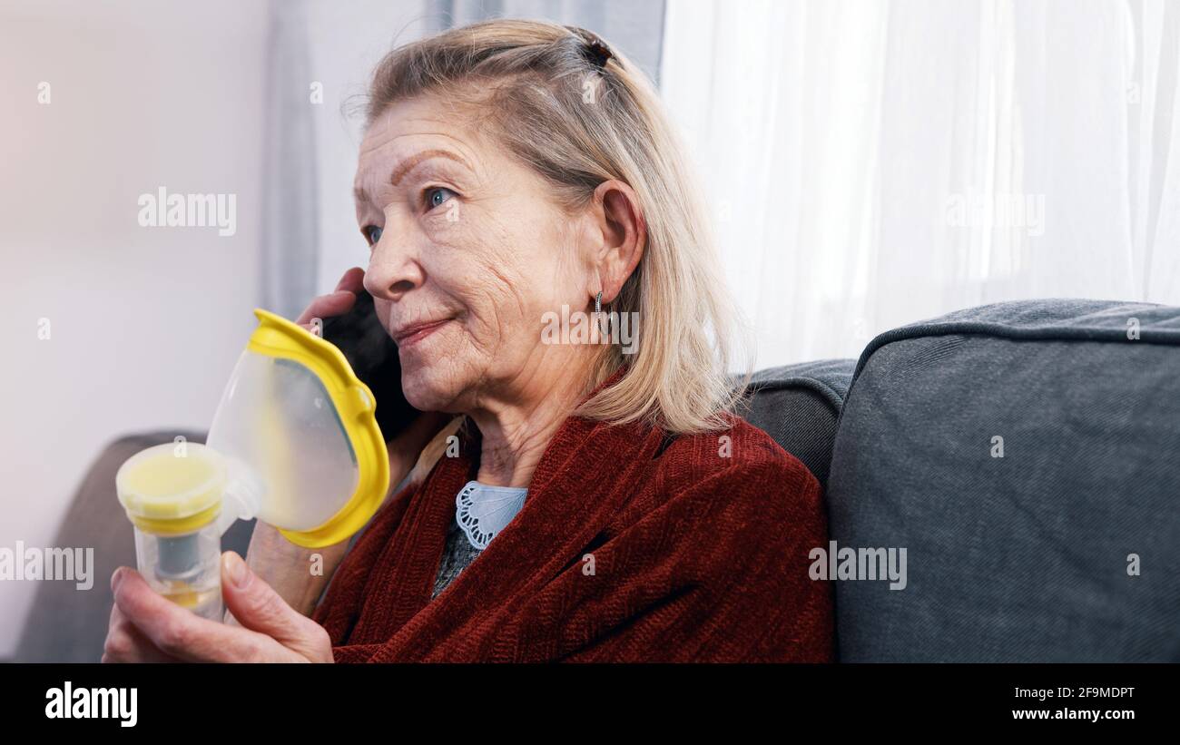Vulnerable old woman having a phone call and using inhaler. Difficulty ...