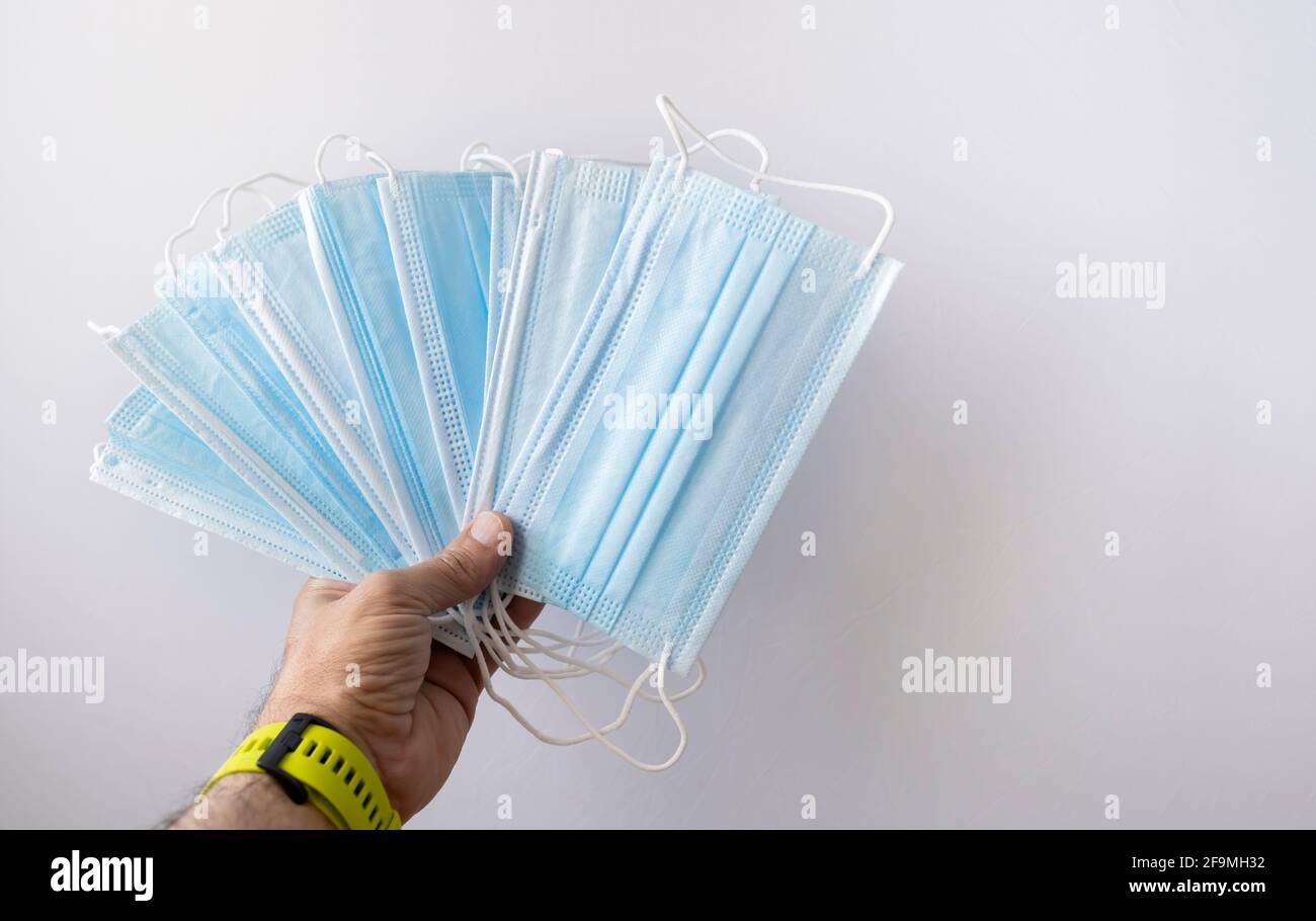 a hand wearing watch with a yellow strap holds a group of surgical face ...