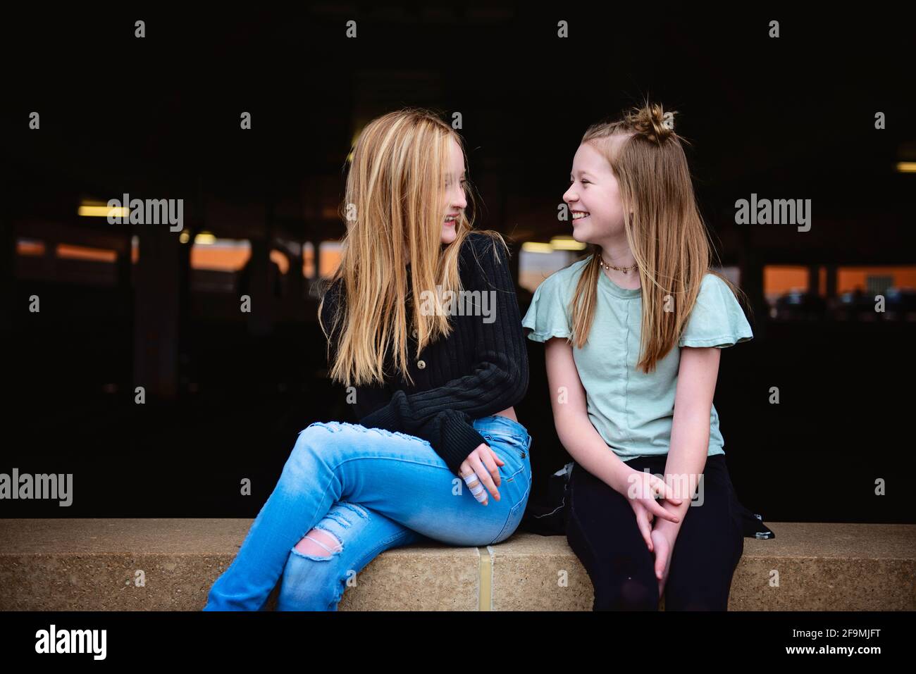 Two happy tween girls sitting on a brick wall together Stock Photo - Alamy