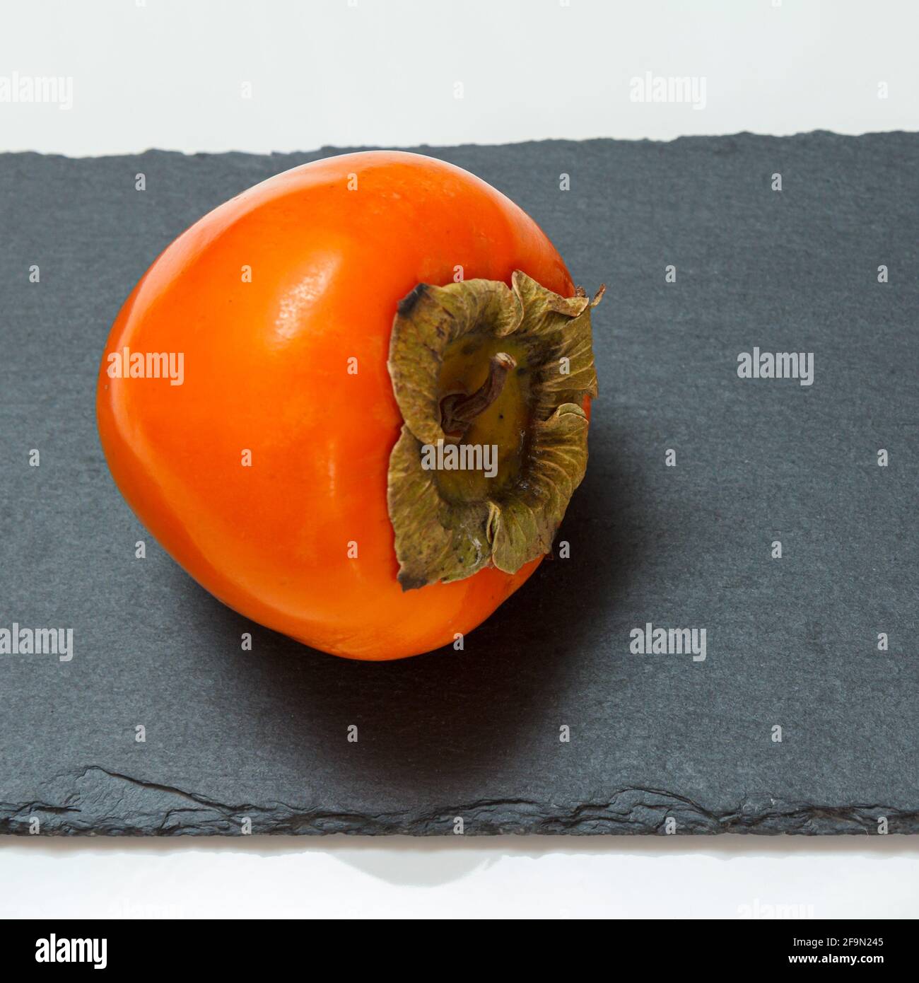 Delicious ripe persimmon fruit on the black stone cutting board ...