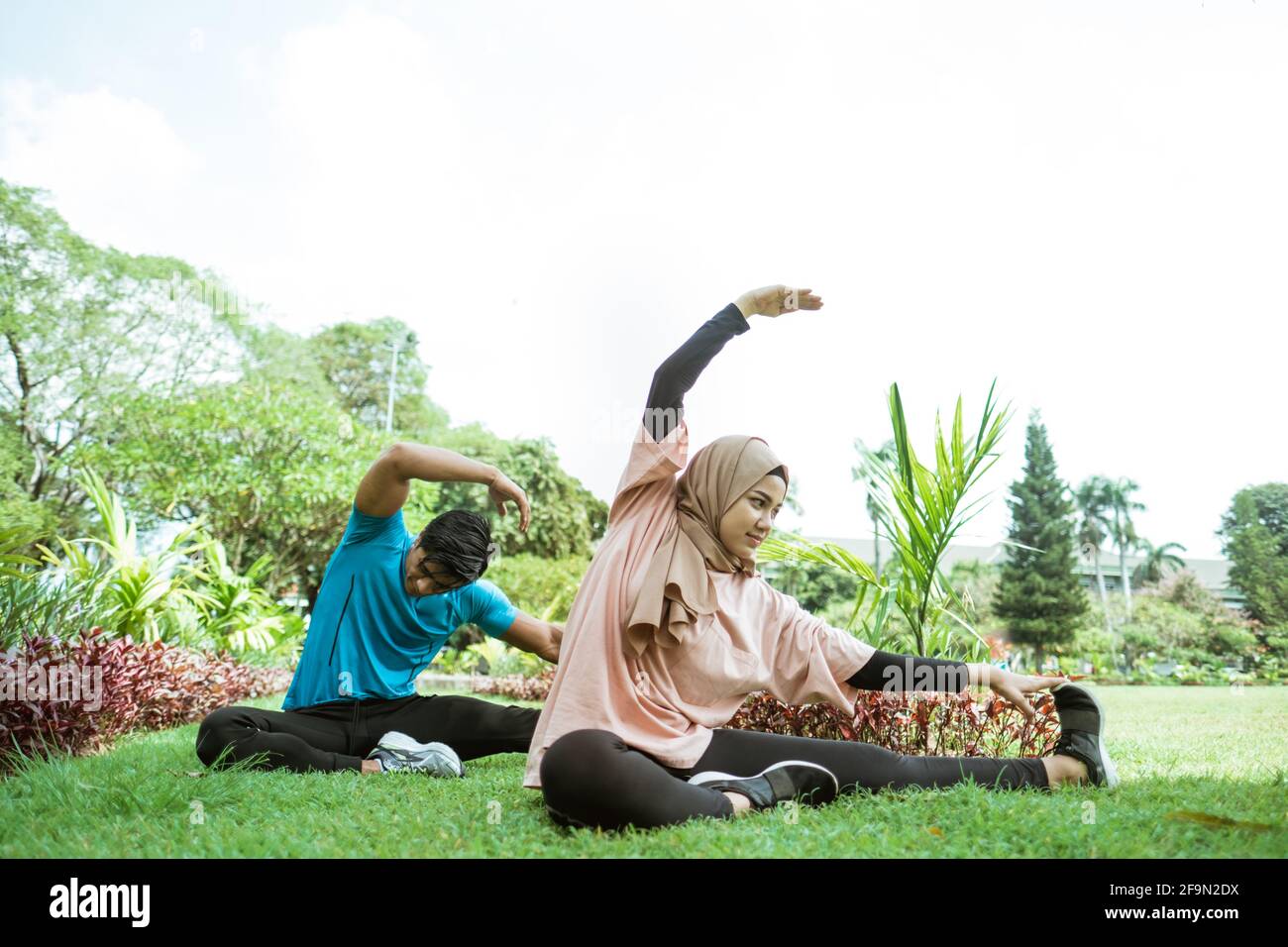 a young man and a girl in a headscarf doing movement to train leg ...
