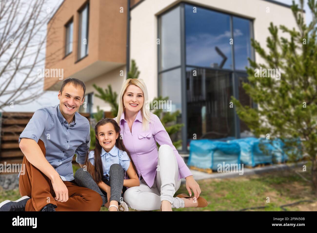 Family sitting on lawn in backyard, big modern house on background ...