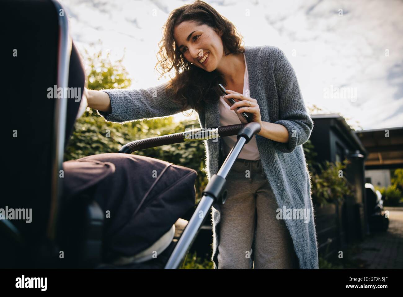 Cheerful mother pushing a stroller and looking at her baby. Happy ...