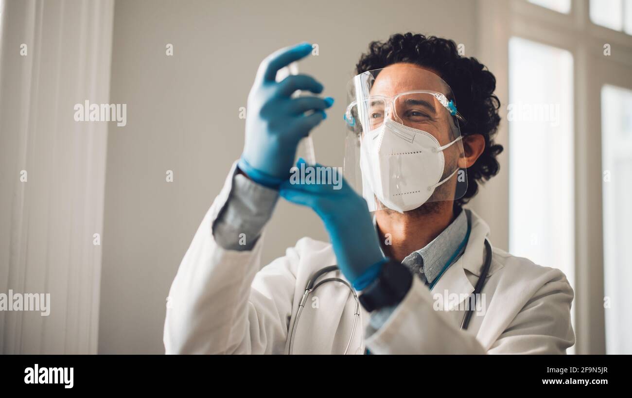 Doctor wearing face mask and face shield filling injection syringe from ...