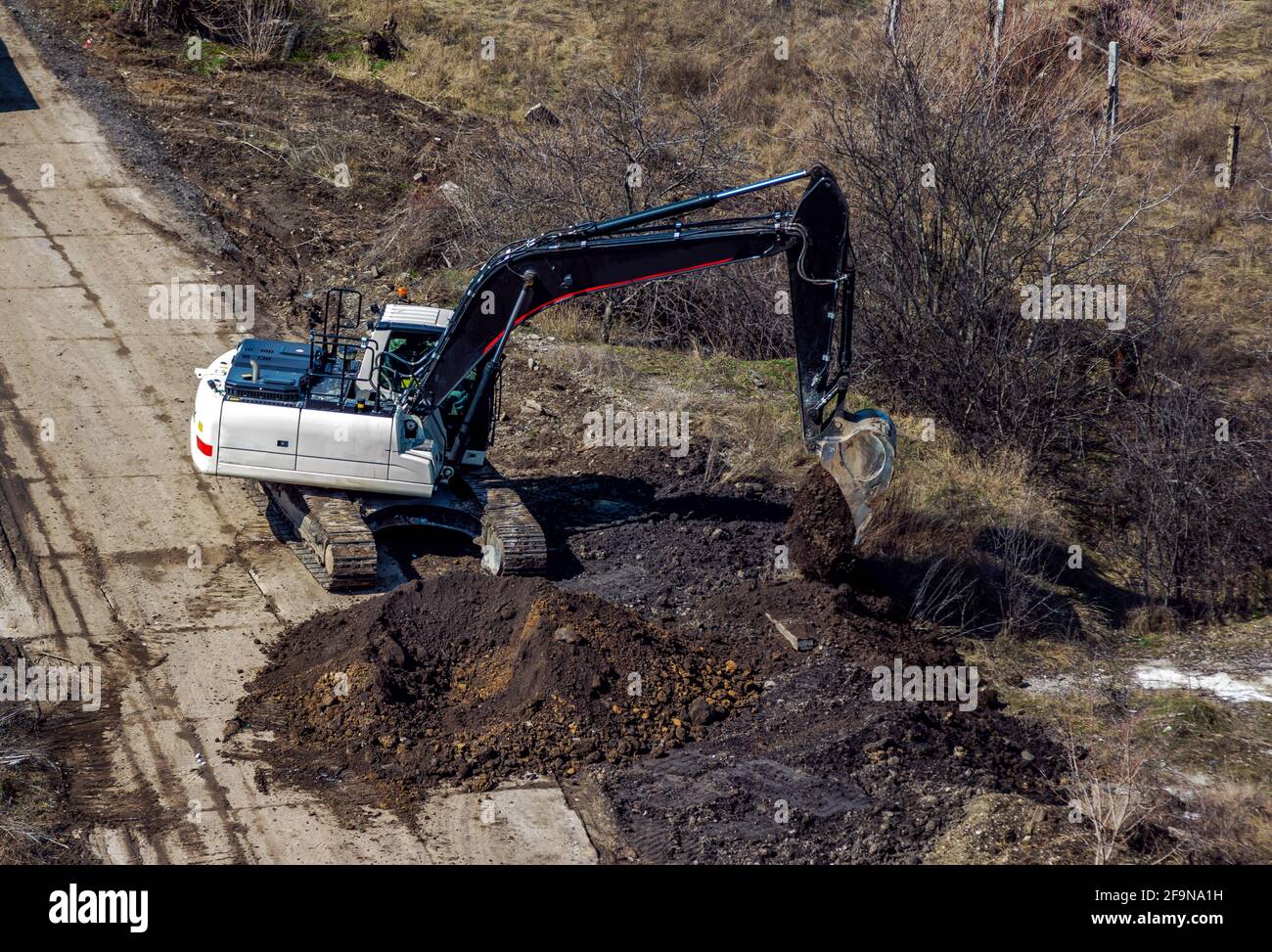 White industrial crawler excavator at work, digging ground, at highway ...