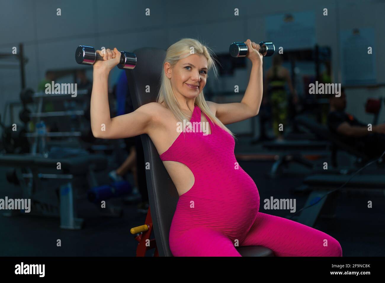 Pregnant woman lifting up dumbbells training arm and shoulders muscle ...