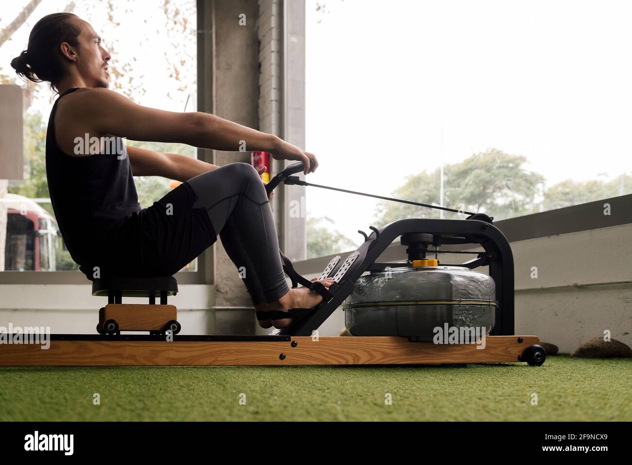 sporty man training his strength in the gym with a water rowing machine ...