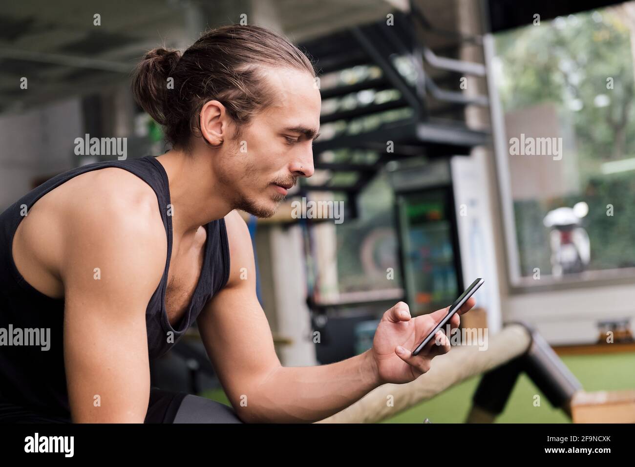 young athlete consulting the phone while resting from his workout at ...