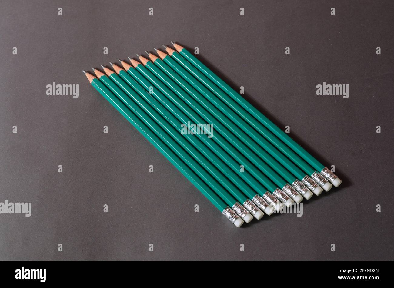 Green pencils on a gray background. A group of new identical wooden pencils are stacked tightly ...