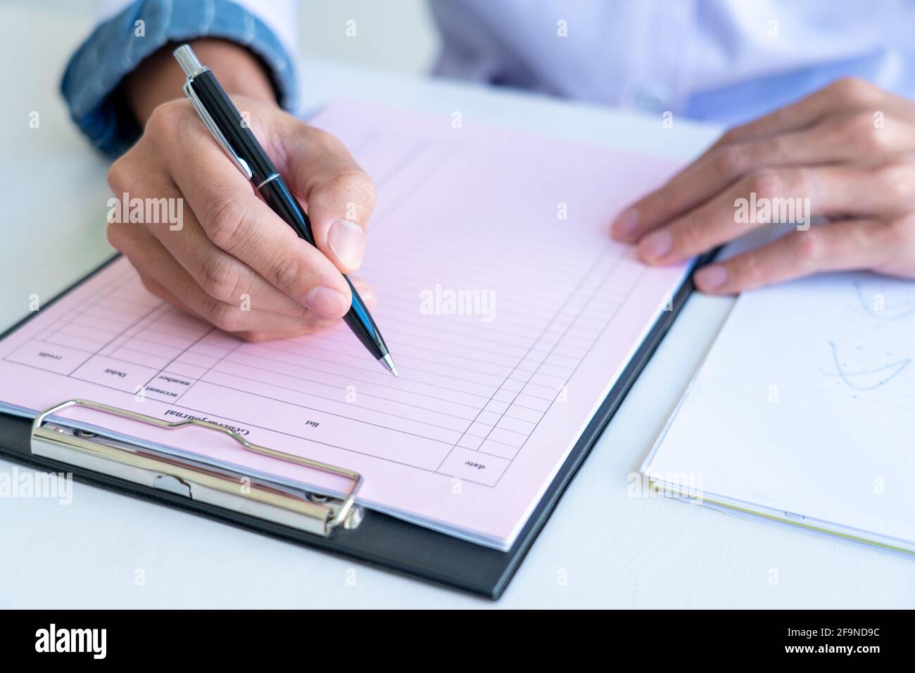 business man works on the table holds pen in right hand and write data ...