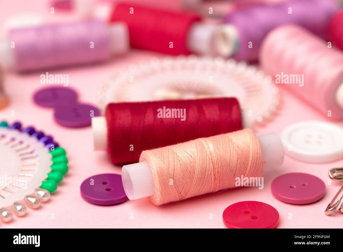 Sewing accessories including thread spools and pins on pink background ...