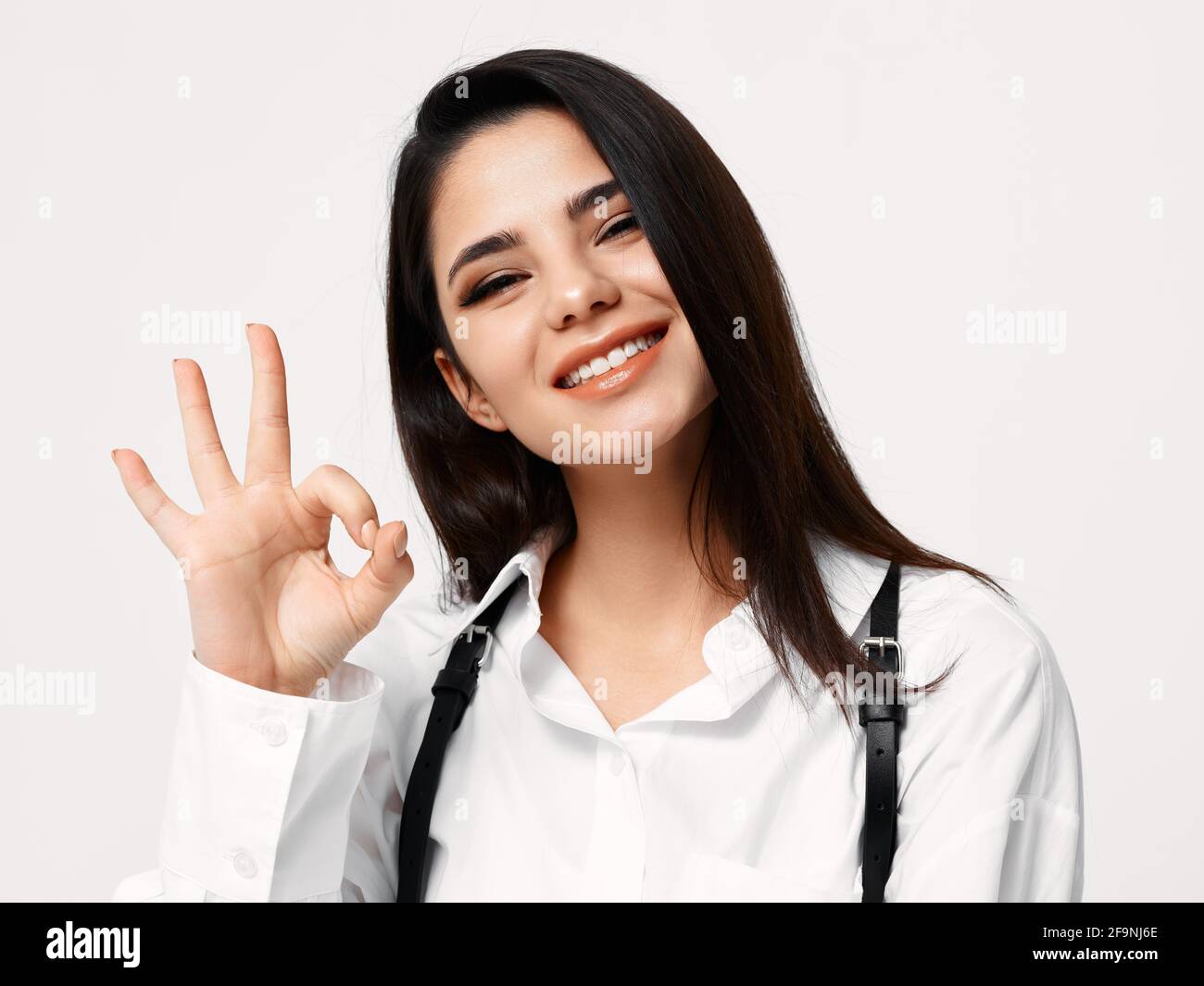 brunette shows a positive gesture with her hand and smiles on a light ...