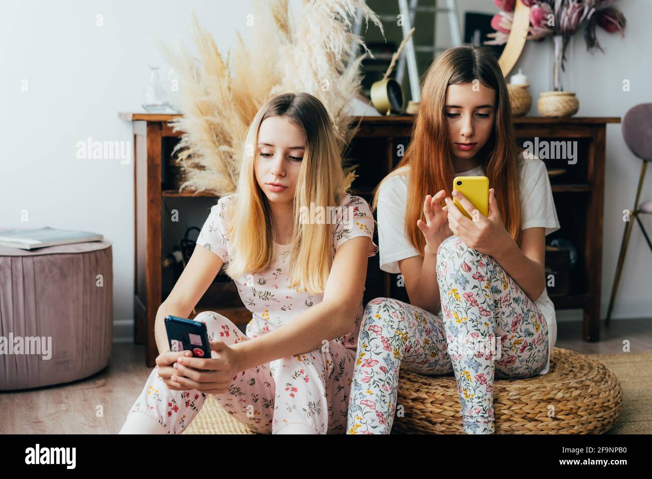 Girls sisters are sitting at home using mobile phones for communication ...