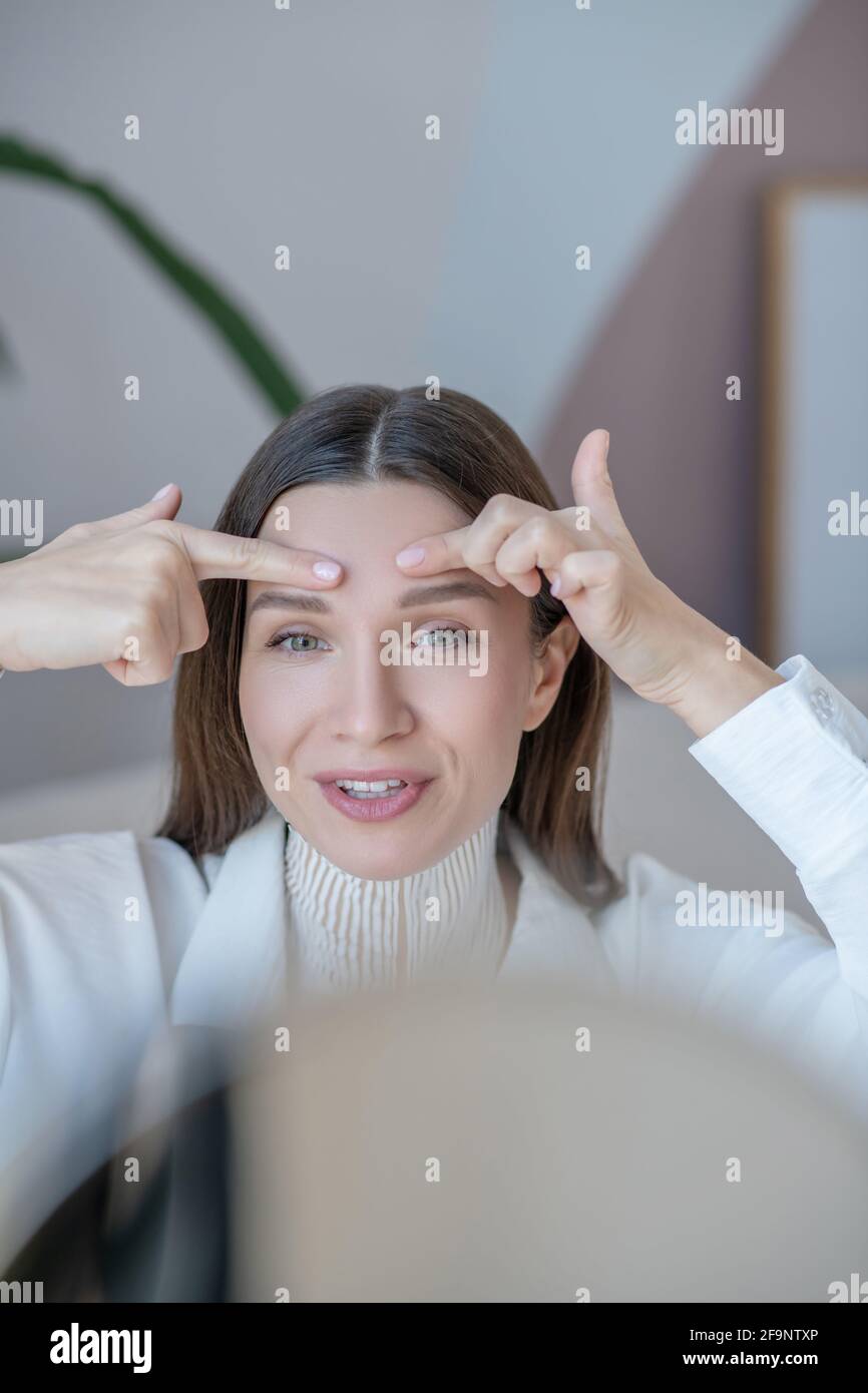 Cute young woman doing face massage in front of the mirror and looking ...