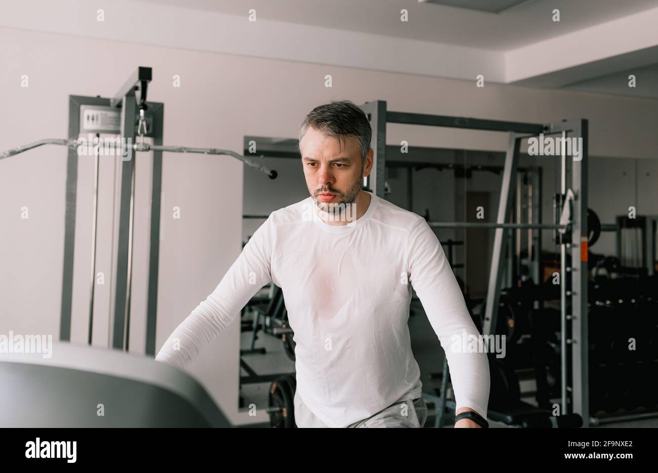a tired man in a sweat-soaked T-shirt runs on a treadmill in a sports ...