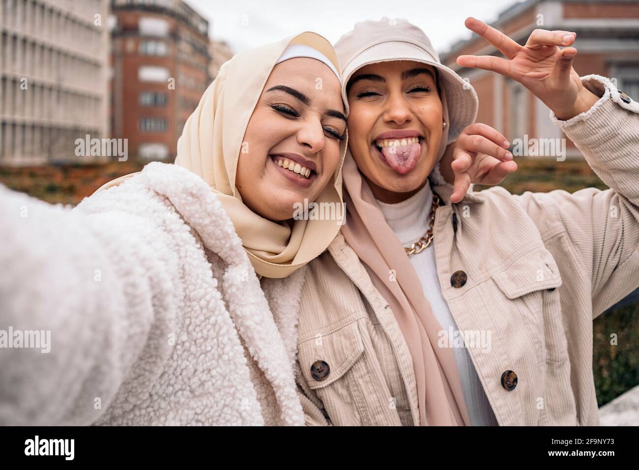 Cheerful girls wearing hijab having fun and taking selfie in the street ...