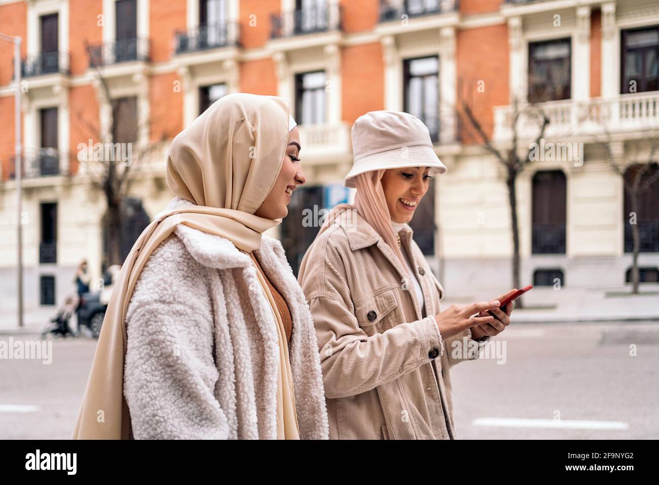 Cheerful girls wearing hijab having fun and using phone in the street ...