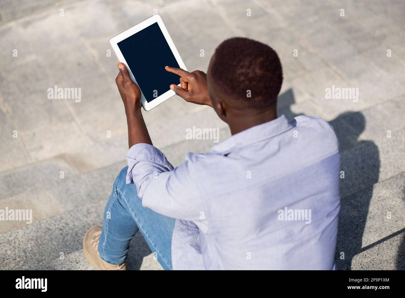 Young black guy using tablet computer with empty screen on stone stairs ...