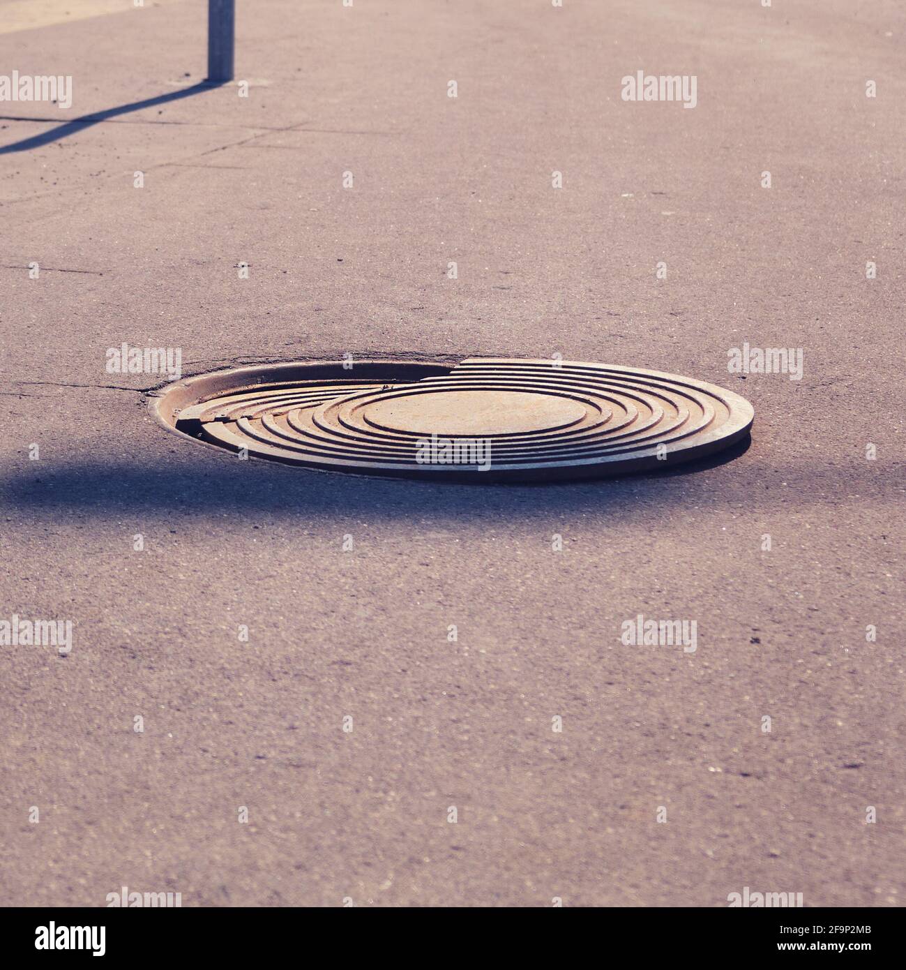 Damaged sewer manhole on the asphalt path, broken metal cover close-up ...