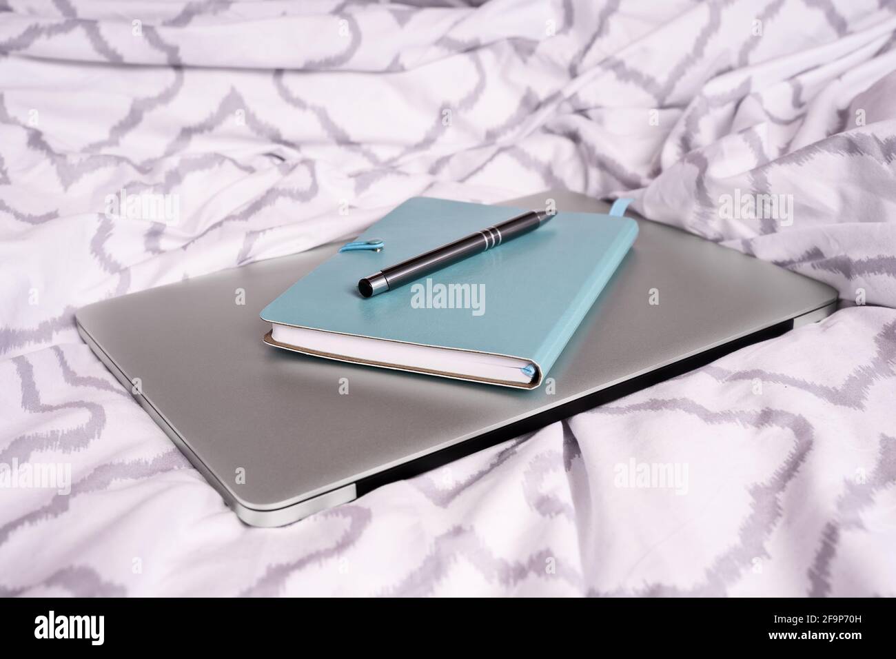 Notepad and pen on top of a laptop computer on bed with modern bright ...