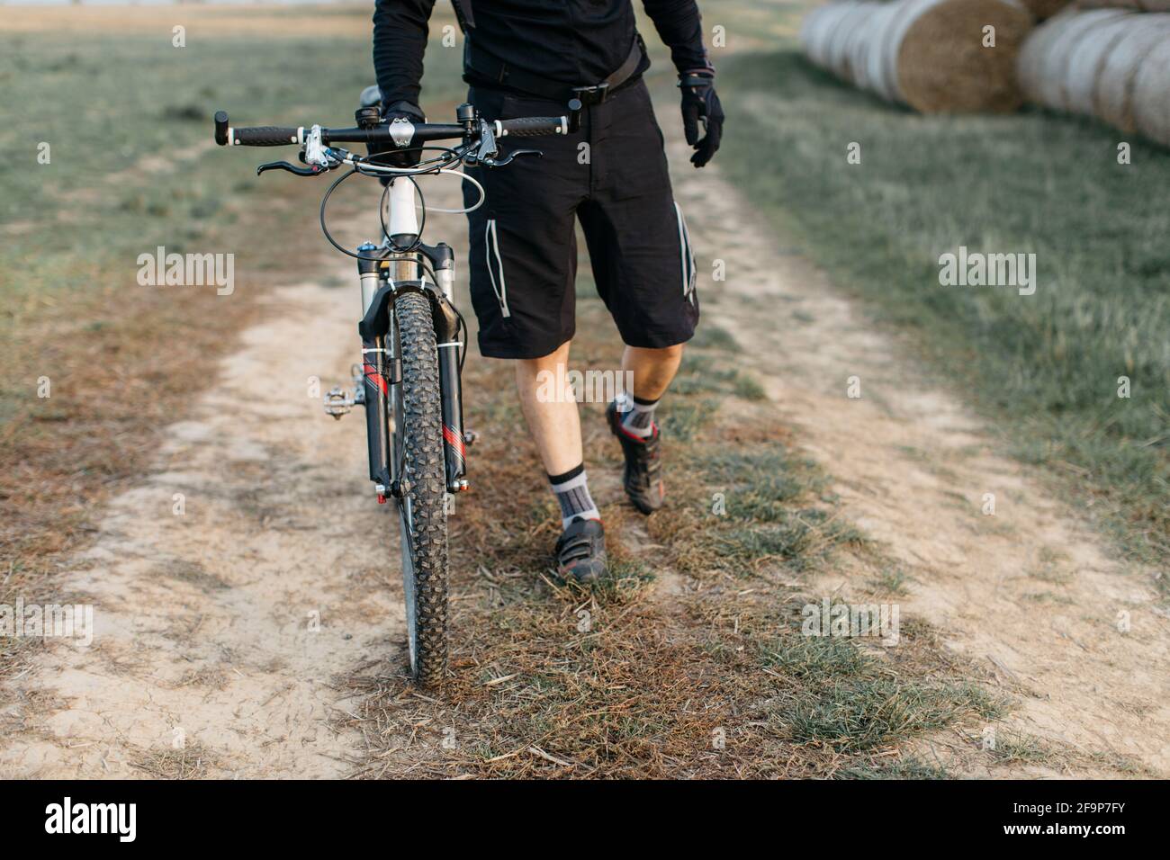 Cyclist pushing mountain bike along dirt track. Front view of biker ...
