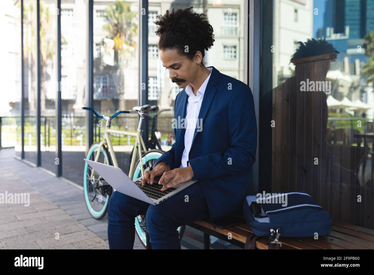Mixed race male with moustache sitting on bench in street using laptop ...