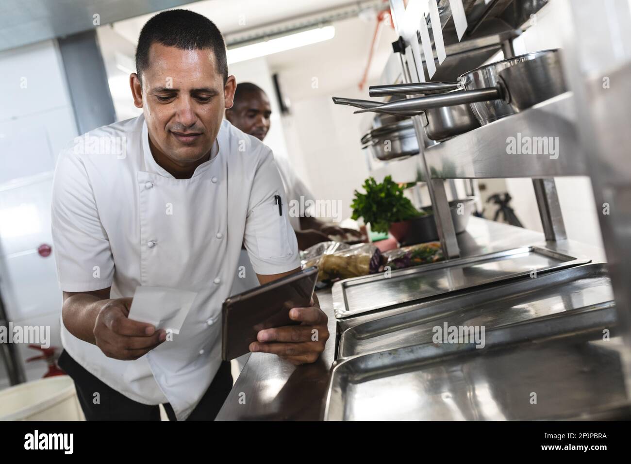 Mixed race professional chef looking at order and tablet with colleague ...