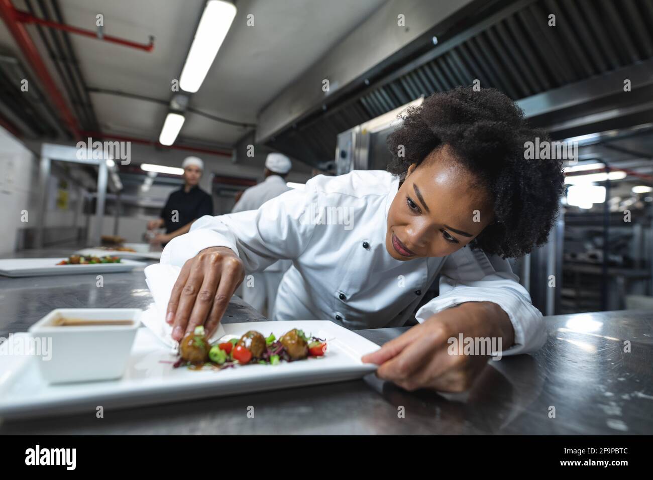 Mixed race professional chef finishing dish before serving with ...