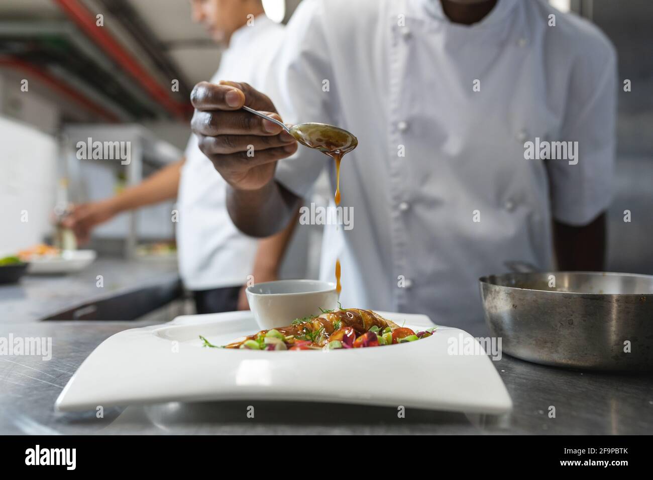 Midsection of mixed race professional chef finishing dish before ...