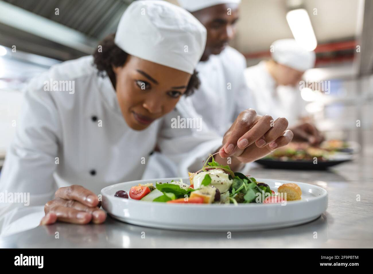 Mixed race professional chef finishing dish before serving with ...