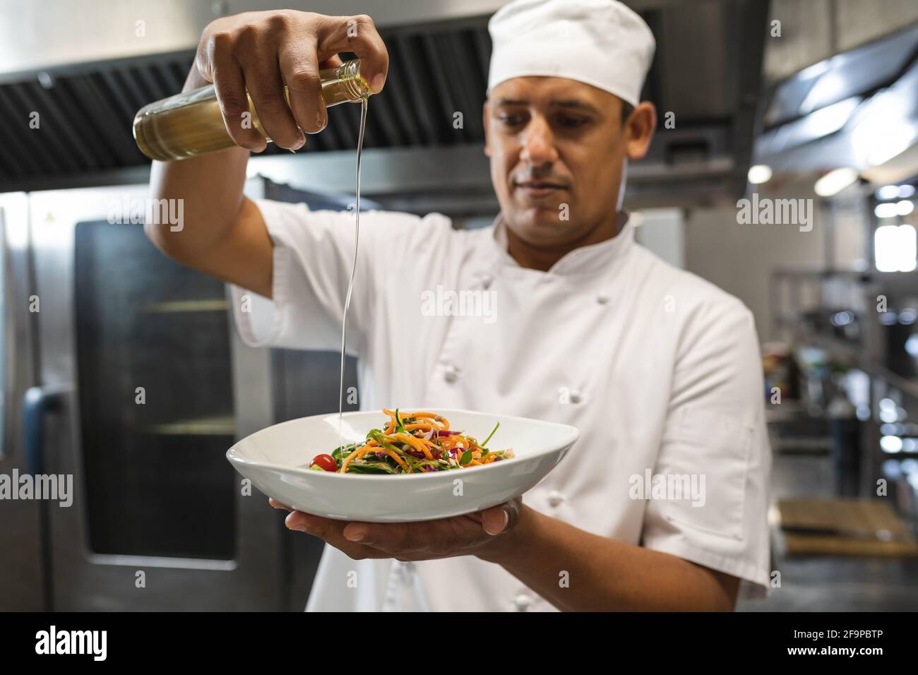 Mixed race male professional chef finishing dish before serving ...