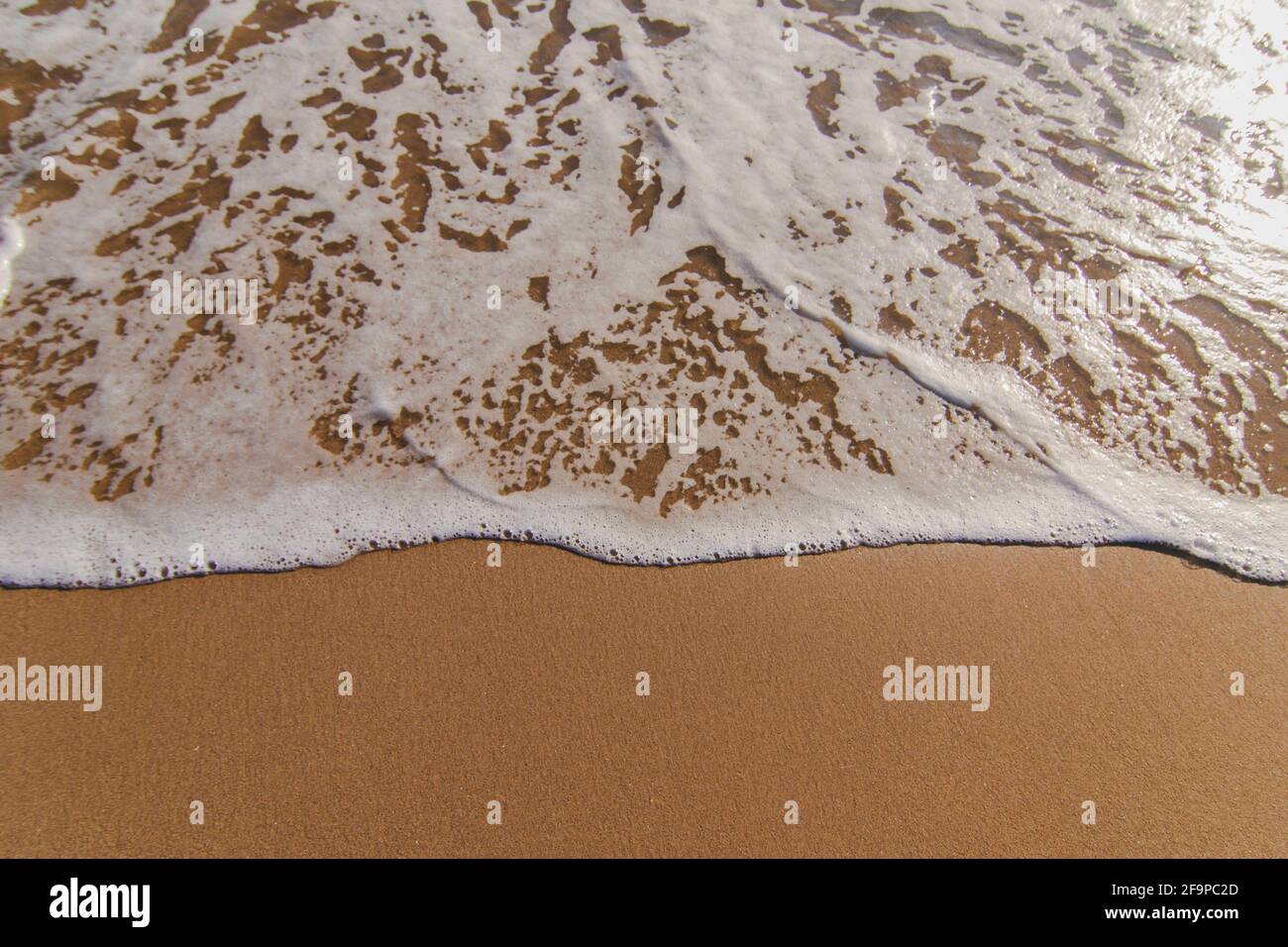 Beautiful shot of white bubbles caused by waves on a sandy beach Stock ...