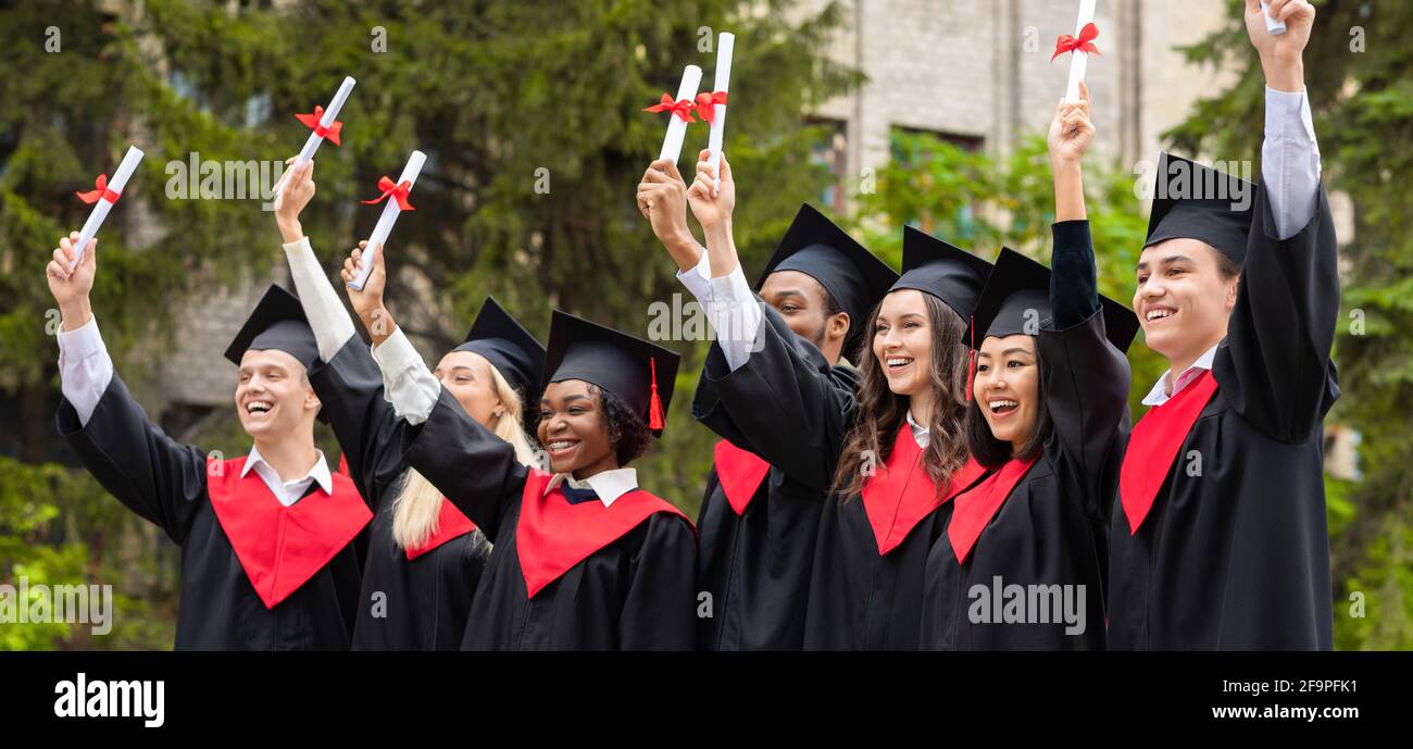 Happy multiracial students in graduation costumes raising diplomas up ...
