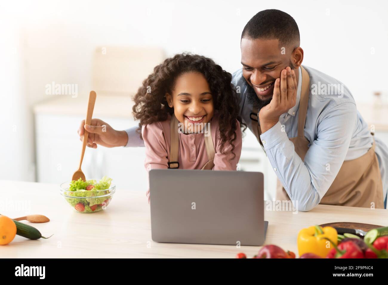 Black man and girl cooking in the kitchen using laptop Stock Photo - Alamy