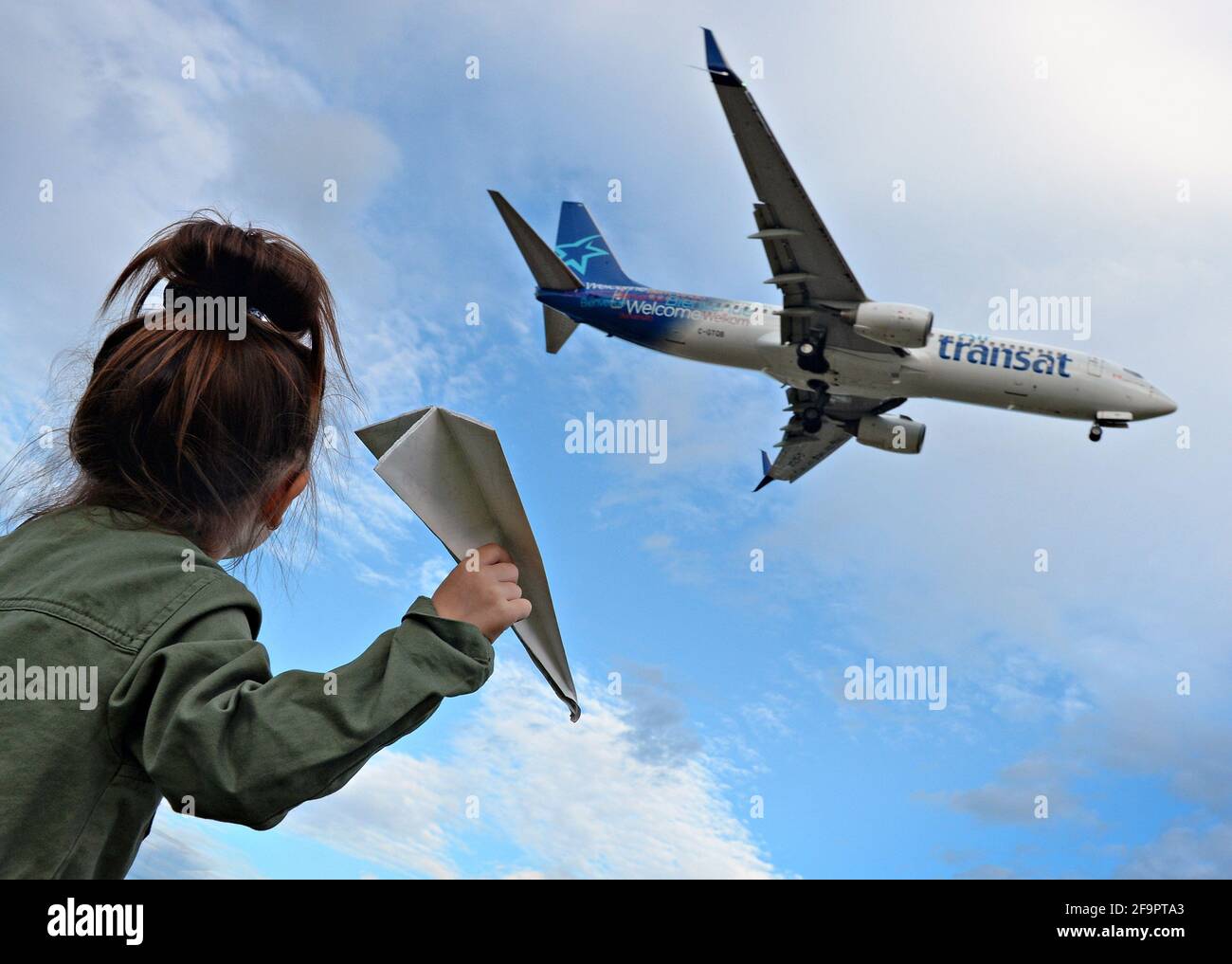 Little girl looks at a plane landing with a paper plane in her hand ...