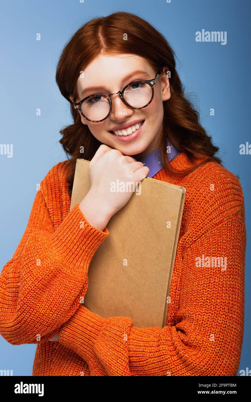 smiling redhead student in glasses and orange sweater holding book ...