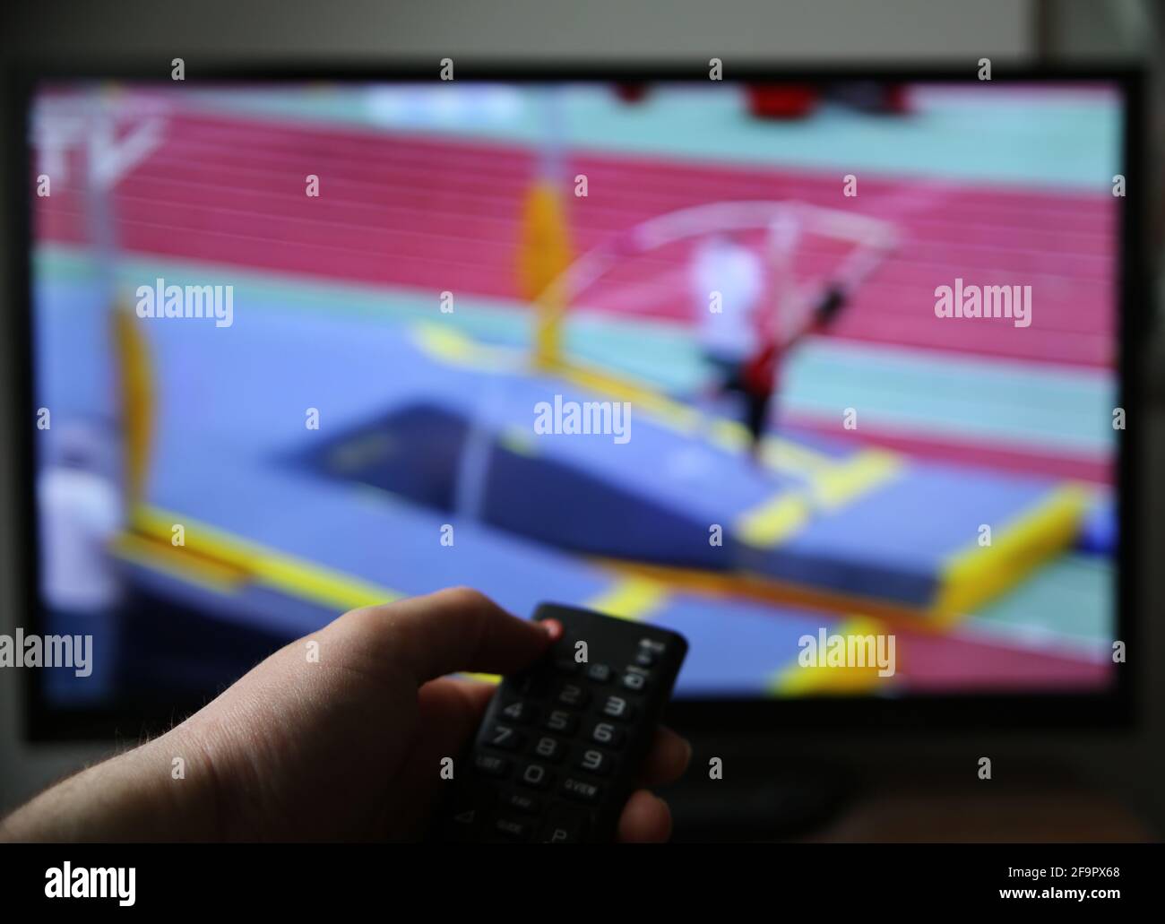 Hand holding the remote controller against the blurred TV screen/Pole ...