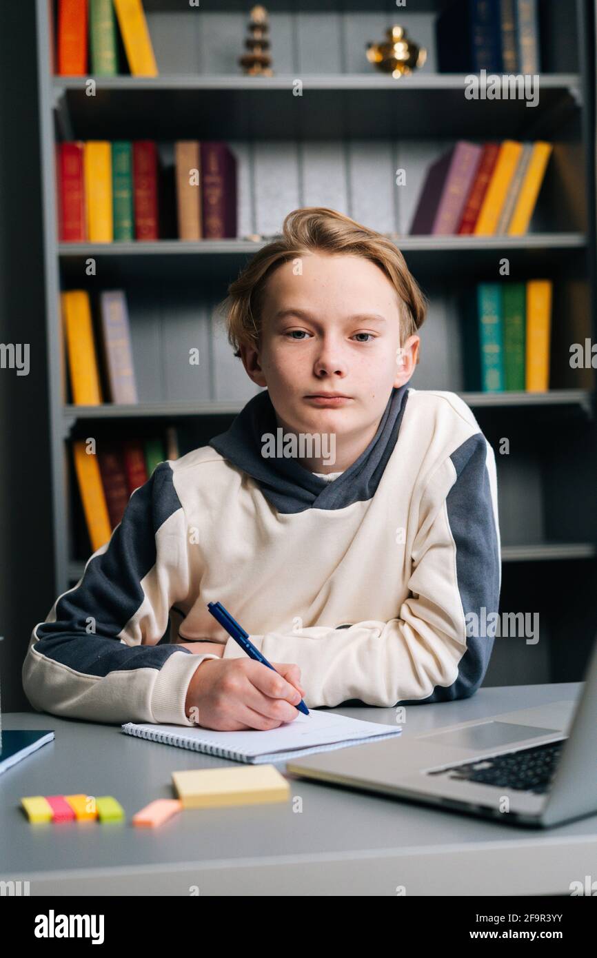 Close-up portrait of pupil boy making notes in notebook with pen ...