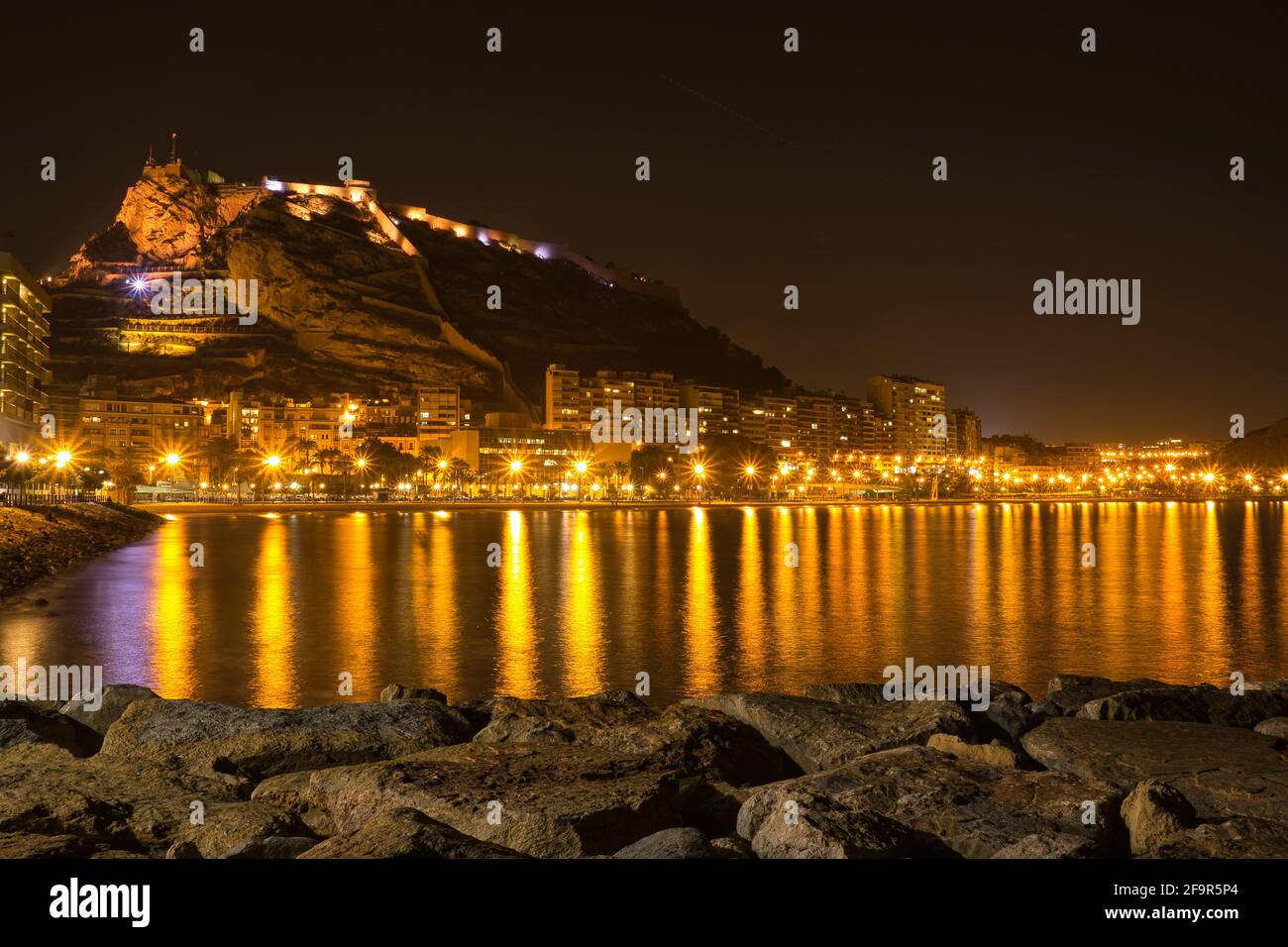 beach at the foot of a castle with reflections of city lights in the ...