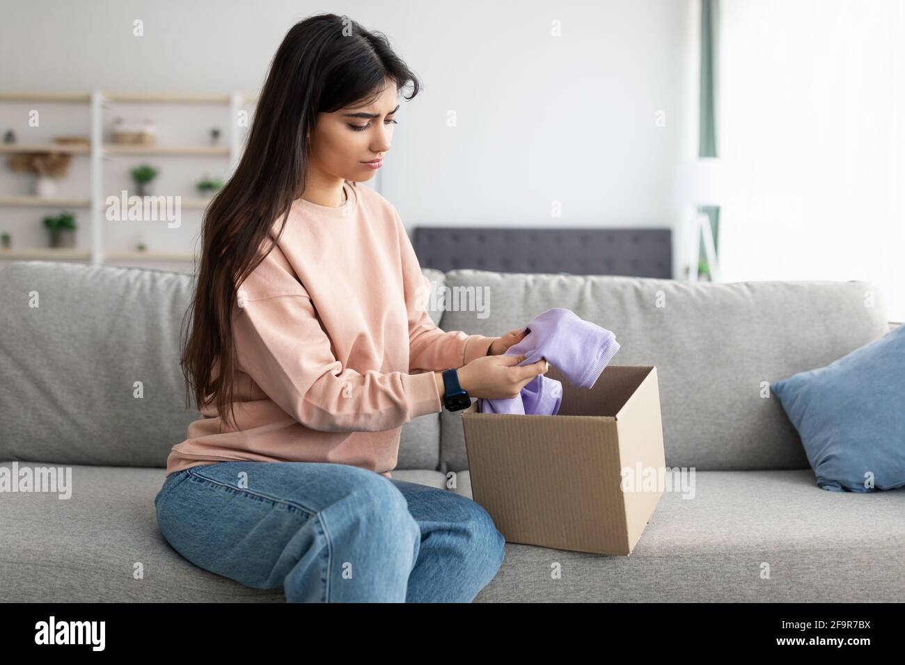 Sad young woman unpacking wrong parcel, delivery mistake Stock Photo ...