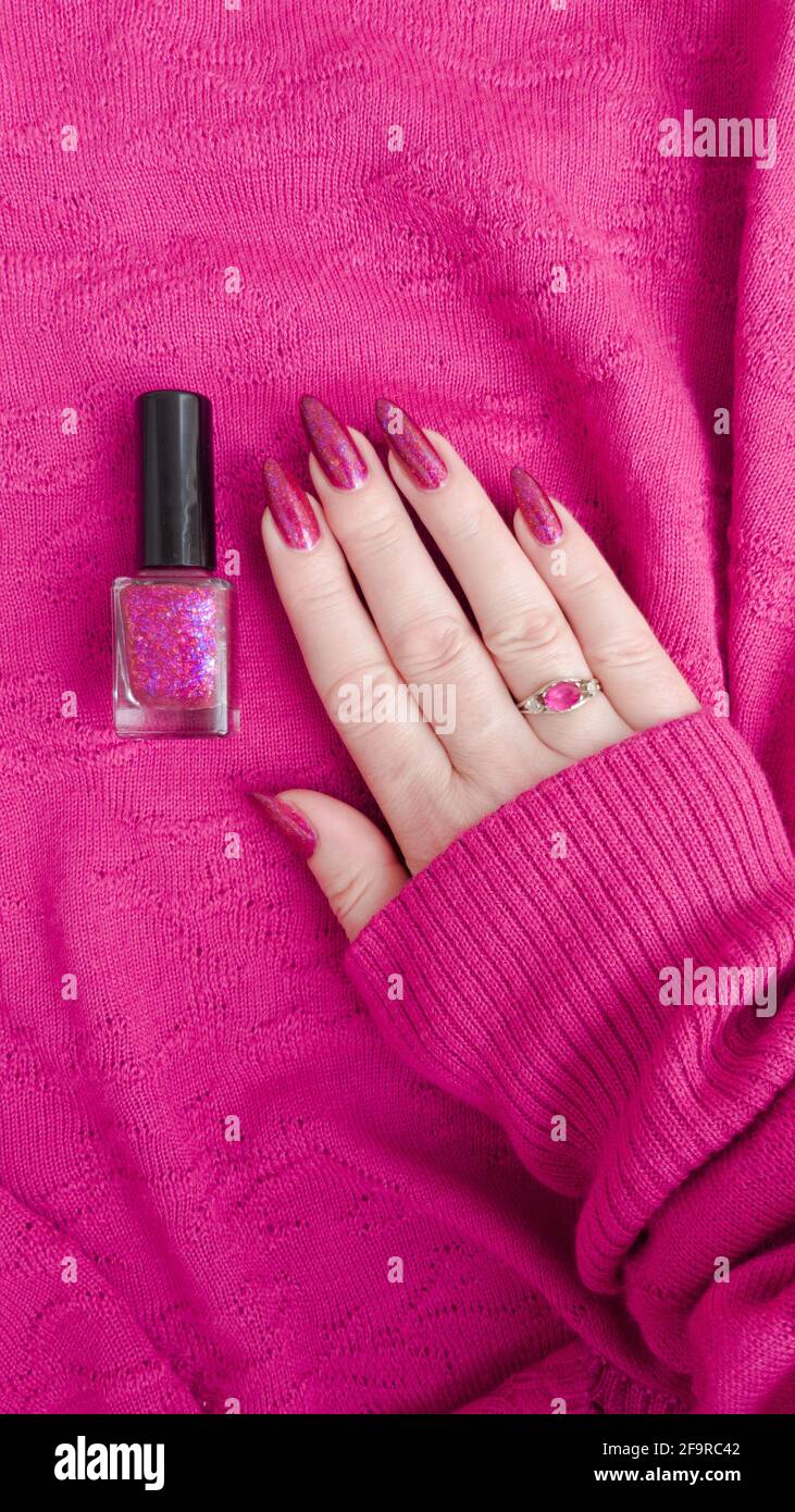 Female hand with long nails and a bottle bright neon pink red color ...