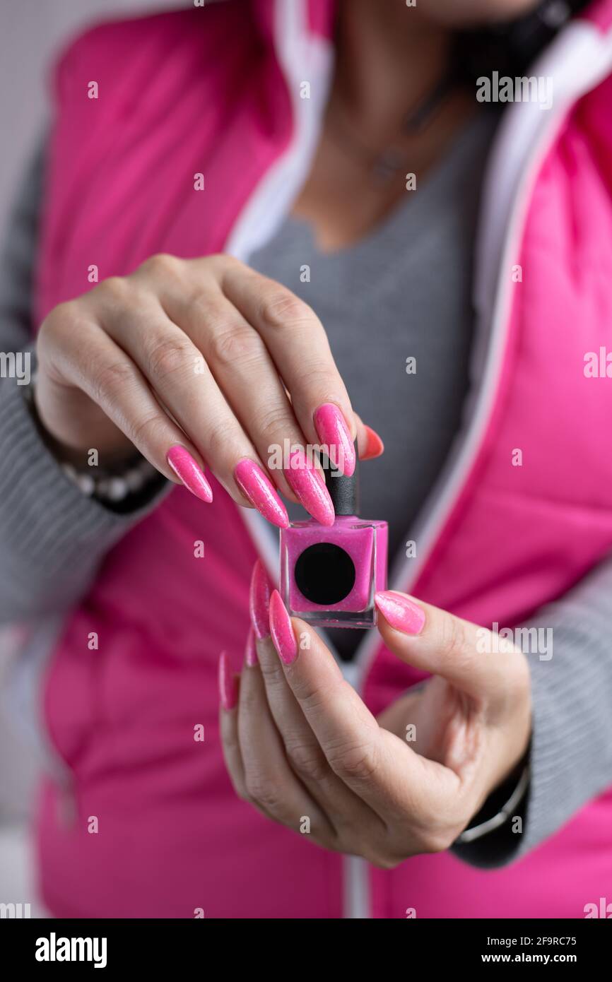 Female hand with long nails and a bottle bright neon pink red color ...