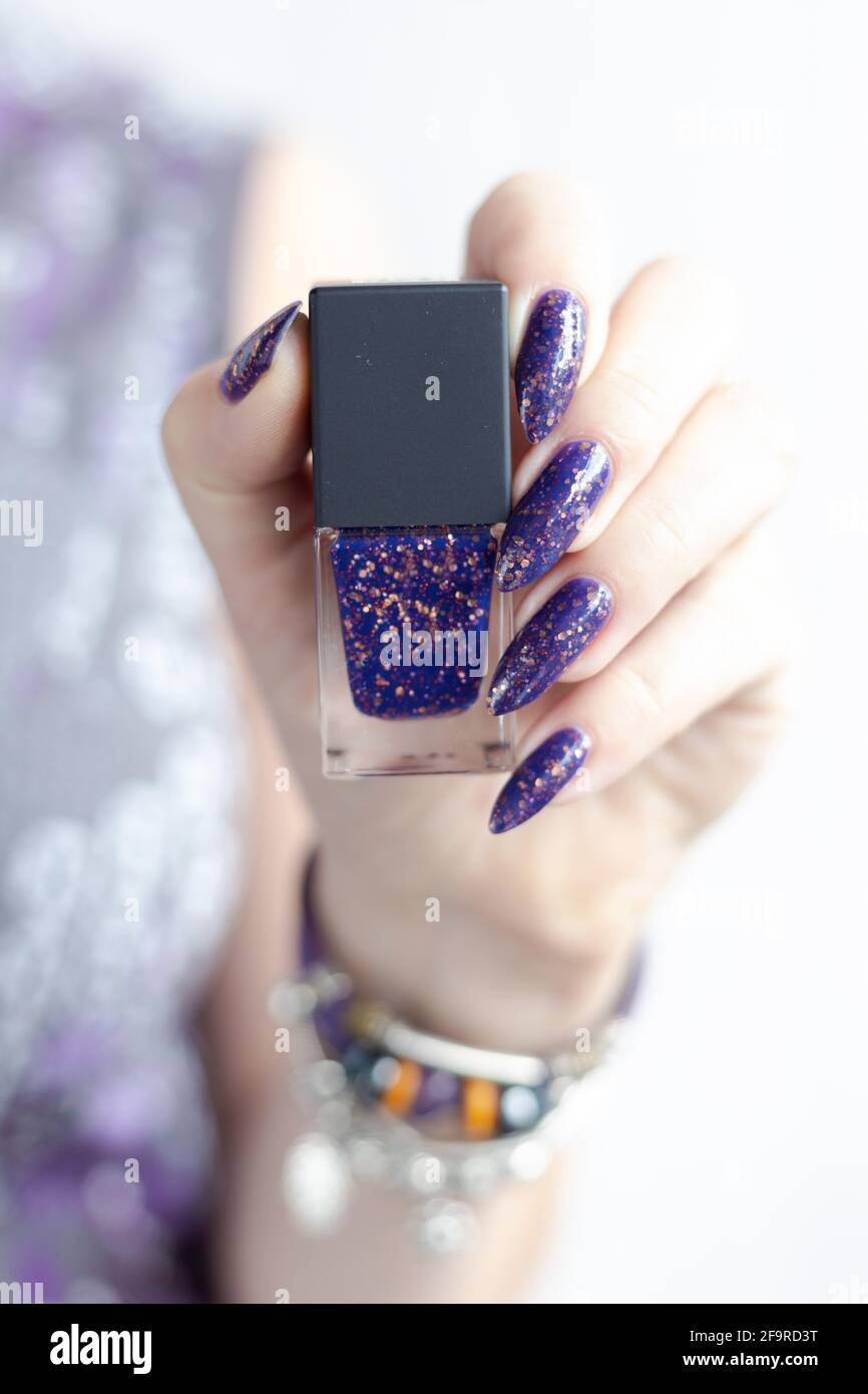 Female hand with long nails and purple lilac manicure holds a bottle of ...