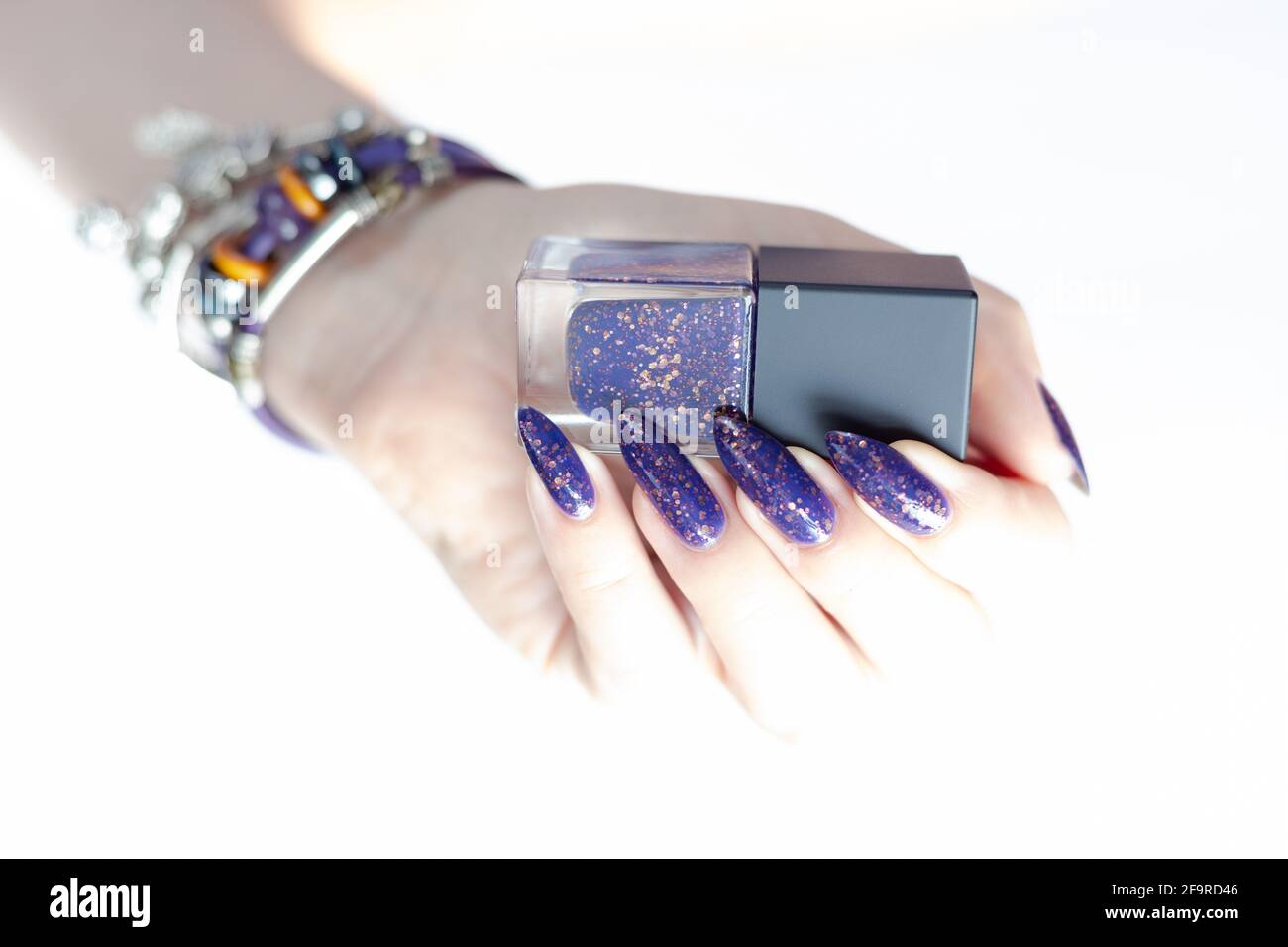 Female hand with long nails and purple lilac manicure holds a bottle of ...