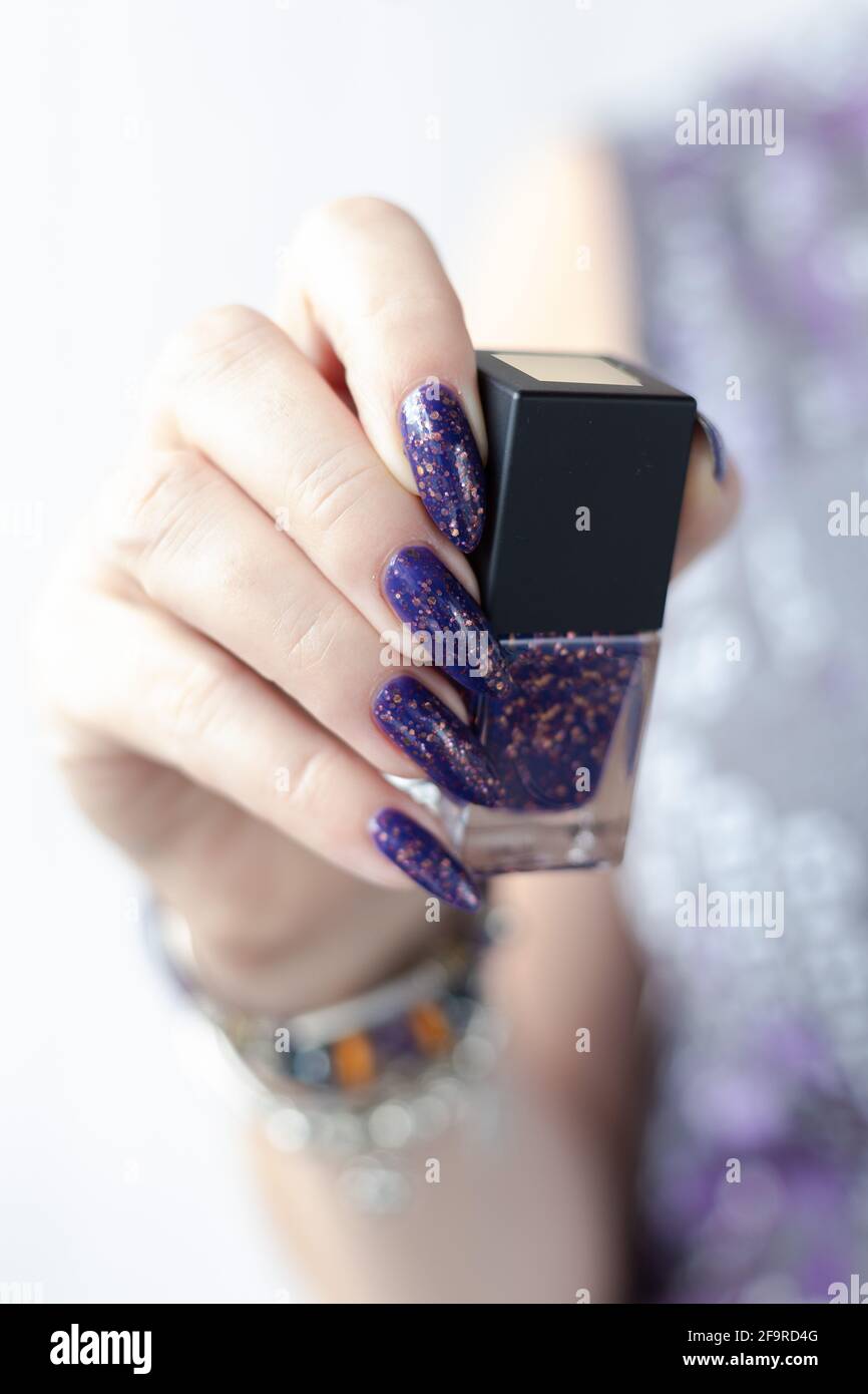 Female hand with long nails and purple lilac manicure holds a bottle of ...